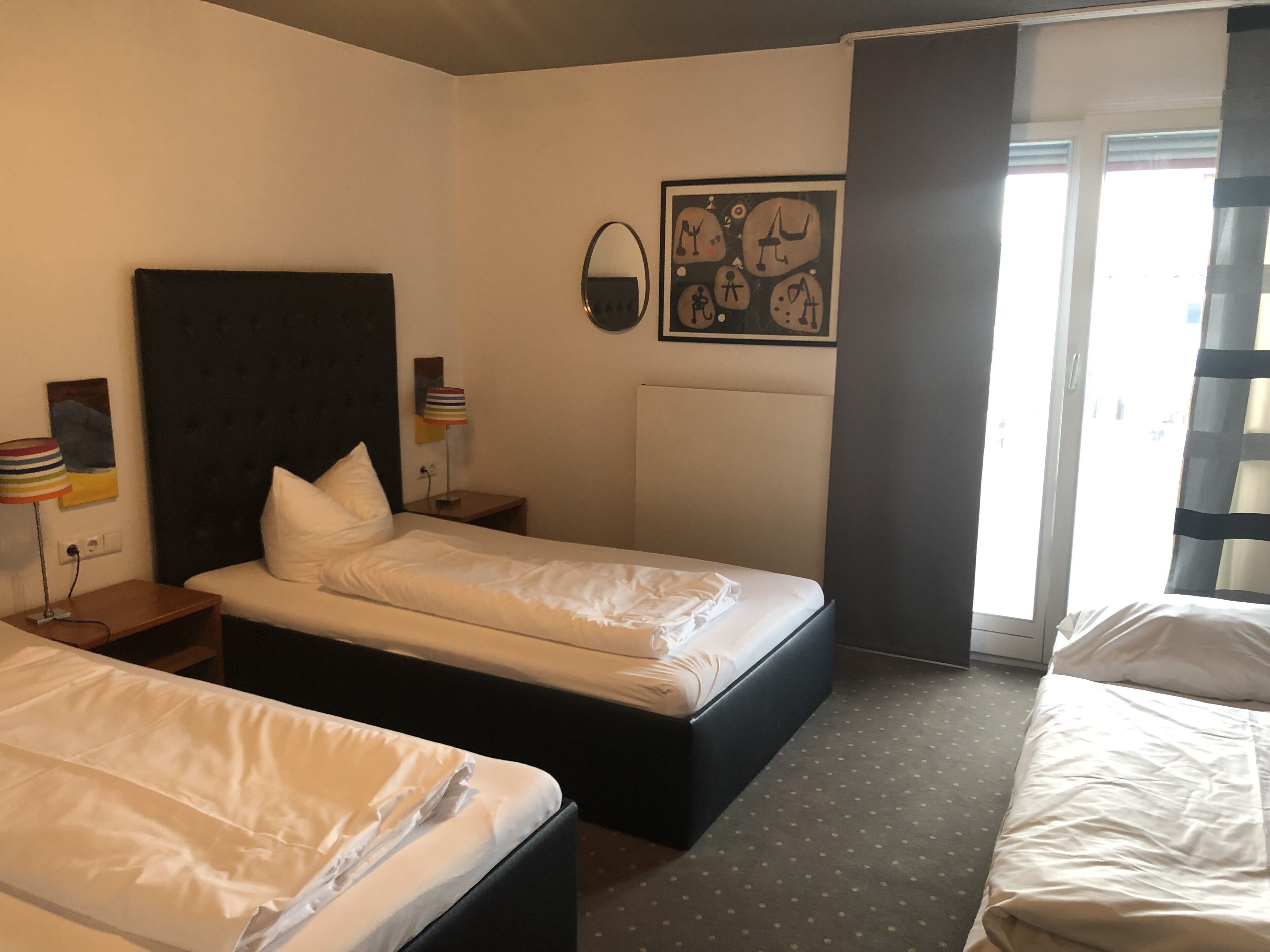 Quarto de hotel com duas camas, um espelho grande e uma janela com cortinas.