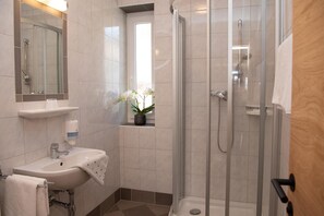 Uma casa de banho moderna com cabine de duche em vidro, lavatório com toalha e espelho.