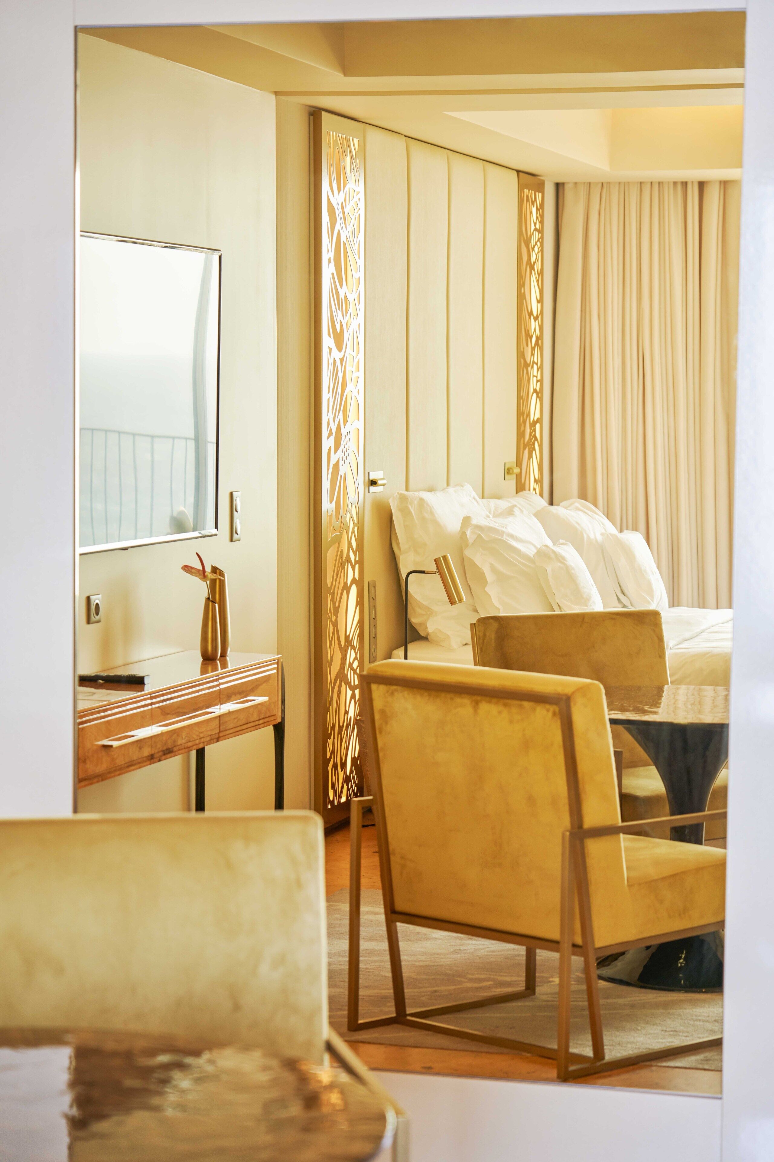 Quarto de hotel com cama, escrivaninha, cadeira e televisão.
