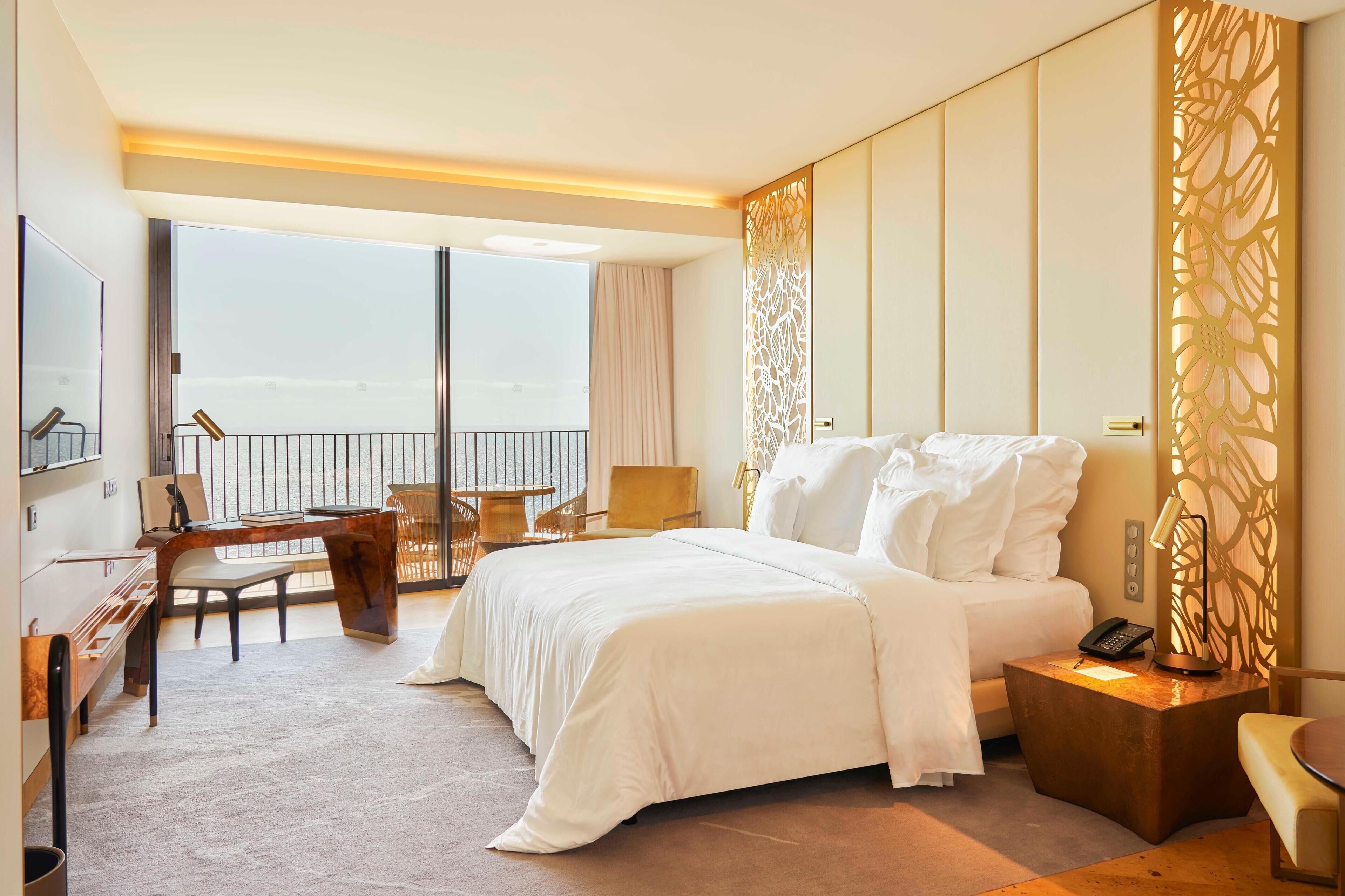 Quarto de hotel com uma cama grande, uma escrivaninha, uma cadeira e vista para o mar.