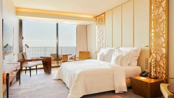 Quarto de hotel com uma cama grande, uma escrivaninha, uma cadeira e vista para o mar.