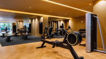 Academia com equipamentos de ginástica, espelhos e um relógio na parede.
