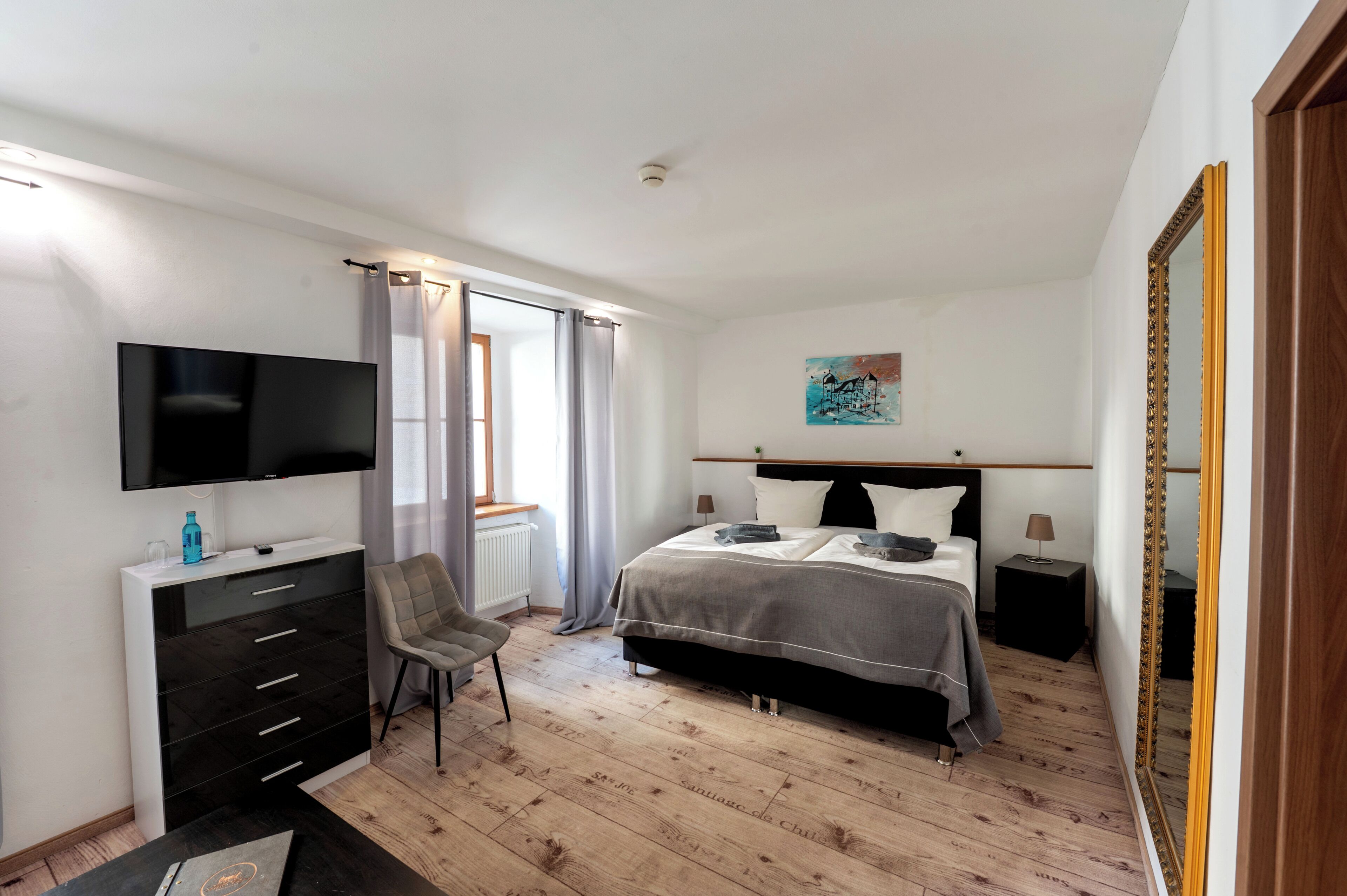 Um quarto com cama, televisão, cômoda, cadeira e um quadro na parede.