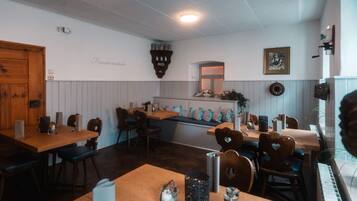 Um restaurante com mesas e cadeiras de madeira, um piano e uma parede com um quadro emoldurado e uma estante com garrafas.