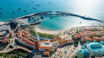 Vista aérea de uma vila costeira com uma ponte notável, uma praça central e uma área de praia.