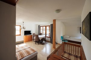 Quarto com cama, escrivaninha, cadeira, televisão e janela.