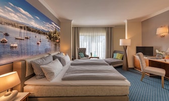 Quarto de hotel com uma cama grande, uma escrivaninha, uma cadeira, uma televisão e vista para barcos na água através de uma janela.