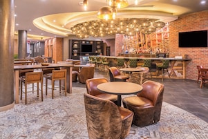 Um restaurante com mesas e cadeiras redondas, um espaço de bar e um chão estampado.