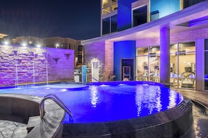 Piscina ao ar livre com muro de pedra e um edifício moderno ao fundo.