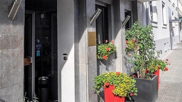 Entrada de um edifício com porta, lixeira e vasos de plantas floridas.