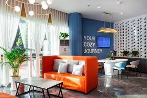 Um hall de hotel moderno com sofá, cadeiras, mesa, TV e uma parede com uma mensagem.