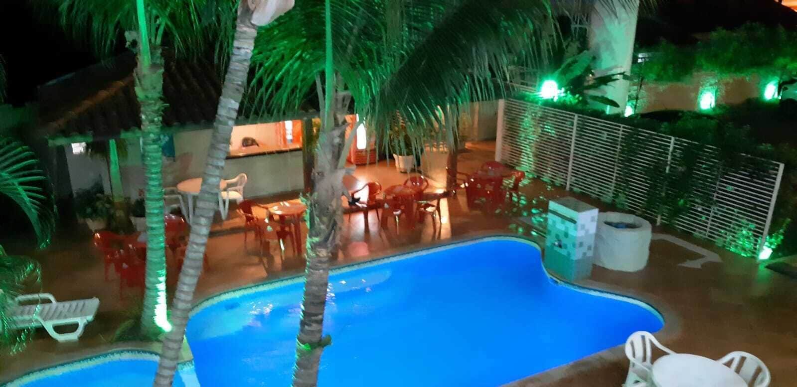 Uma área de piscina com borda curva, cercada por palmeiras e cadeiras vermelhas.