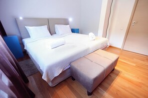 Cama bem arrumada com cabeceira, mesa de cabeceira e um banquinho.
