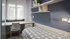 Quarto com cama, escrivaninha, cadeira, janela e prateleiras embutidas.