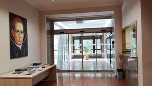 Um hall de entrada com balcão de recepção, uma grande pintura, porta de vidro e um vaso com planta.