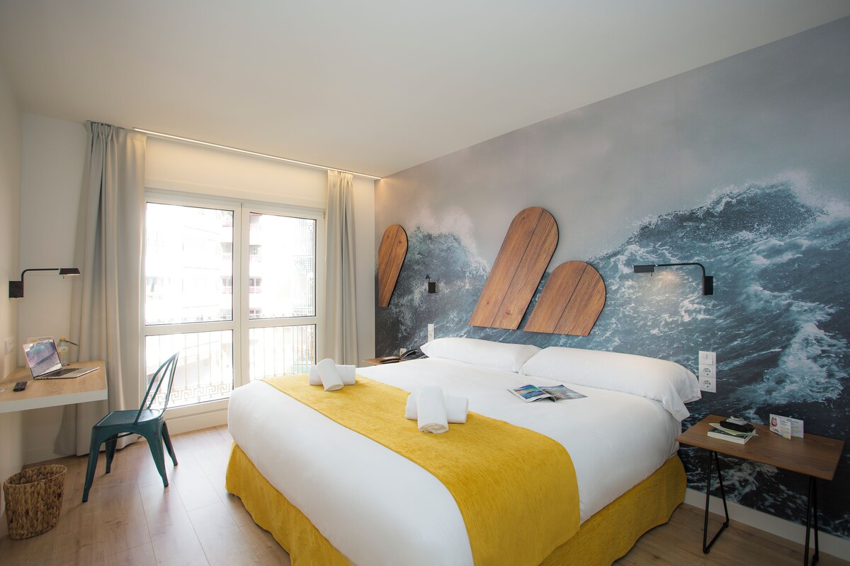 Quarto de hotel com uma cama, uma escrivaninha e uma cadeira.