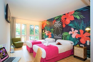 Quarto de hotel com duas camas, um laptop, uma cadeira, uma mesinha de cabeceira e um grande mural floral na parede.