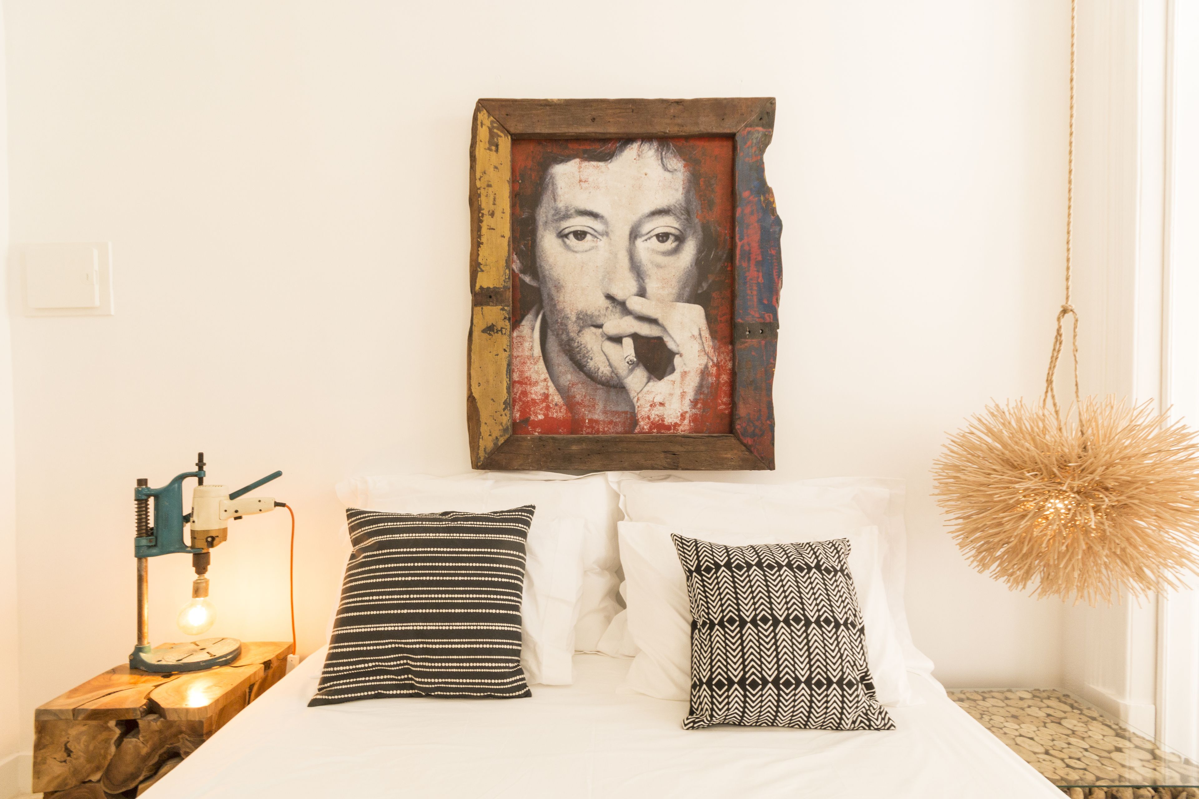 Quarto com cama, abajur, luminária pendente e uma obra de arte emoldurada na parede.