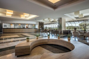 Um lobby moderno com balcão de recepção, área de estar e uma grande janela com vista para o exterior.