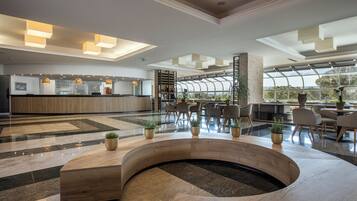 Um lobby moderno com balcão de recepção, área de estar e uma grande janela com vista para o exterior.