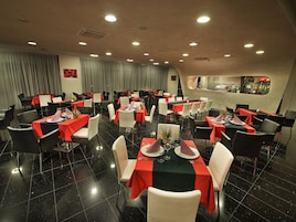 Um restaurante com várias mesas, cada uma com cadeiras brancas e toalhas vermelhas.