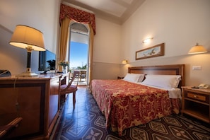 Quarto de hotel com cama, escrivaninha, cadeira e vista para o exterior.