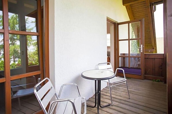 Uma área de estar ao ar livre coberta, com mesa, cadeiras, janelas amplas e um deck de madeira.