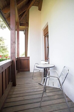 Uma varanda de madeira com mesa e cadeiras, guarda-corpo de madeira e uma janela com persianas.