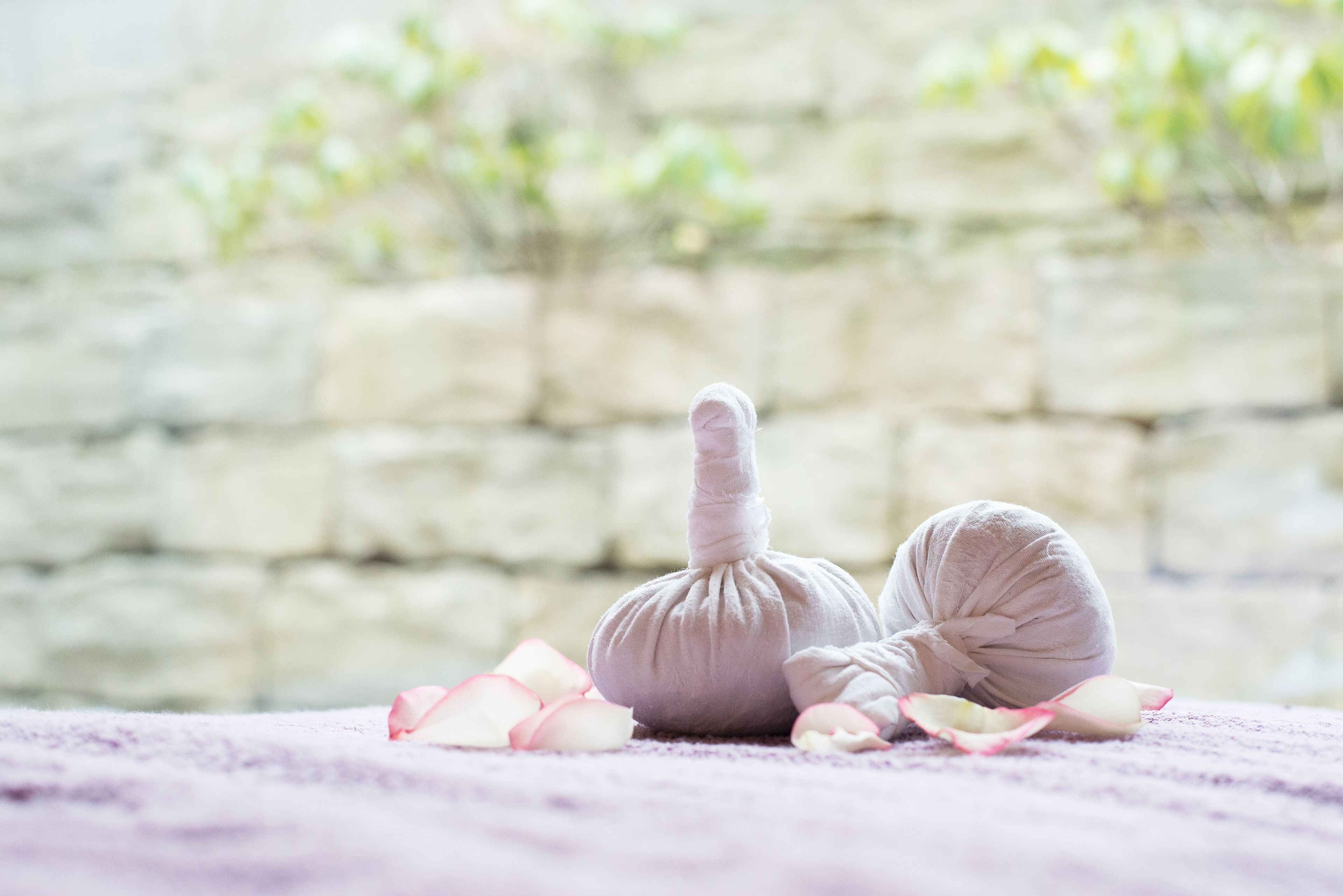Pedra de massagem e toalha enrolada sobre superfície roxa com pétalas de rosa.
