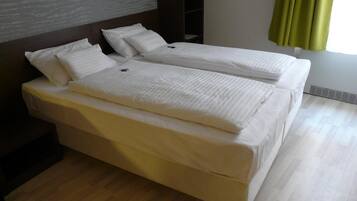Uma cama de casal com roupa de cama branca, cabeceira de madeira e estante embutida.