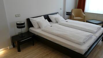 Uma cama de casal com lençóis brancos, uma mesa de cabeceira com abajur e uma cadeira em um quarto de hotel.