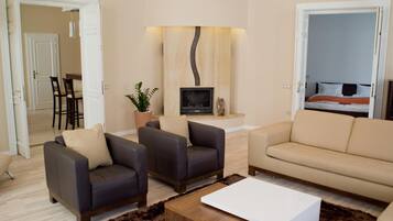 Uma sala de estar moderna com um sofá, duas poltronas, uma mesa de centro, uma televisão e uma lareira.