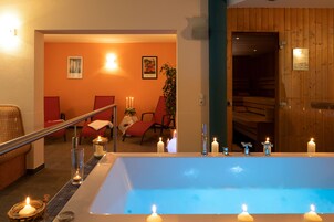Uma área de spa com uma banheira grande, paredes de madeira e um espaço de estar com cadeiras e uma mesa.