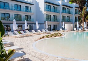 Área de piscina com espreguiçadeiras e guarda-sóis, uma piscina e um edifício com várias varandas.