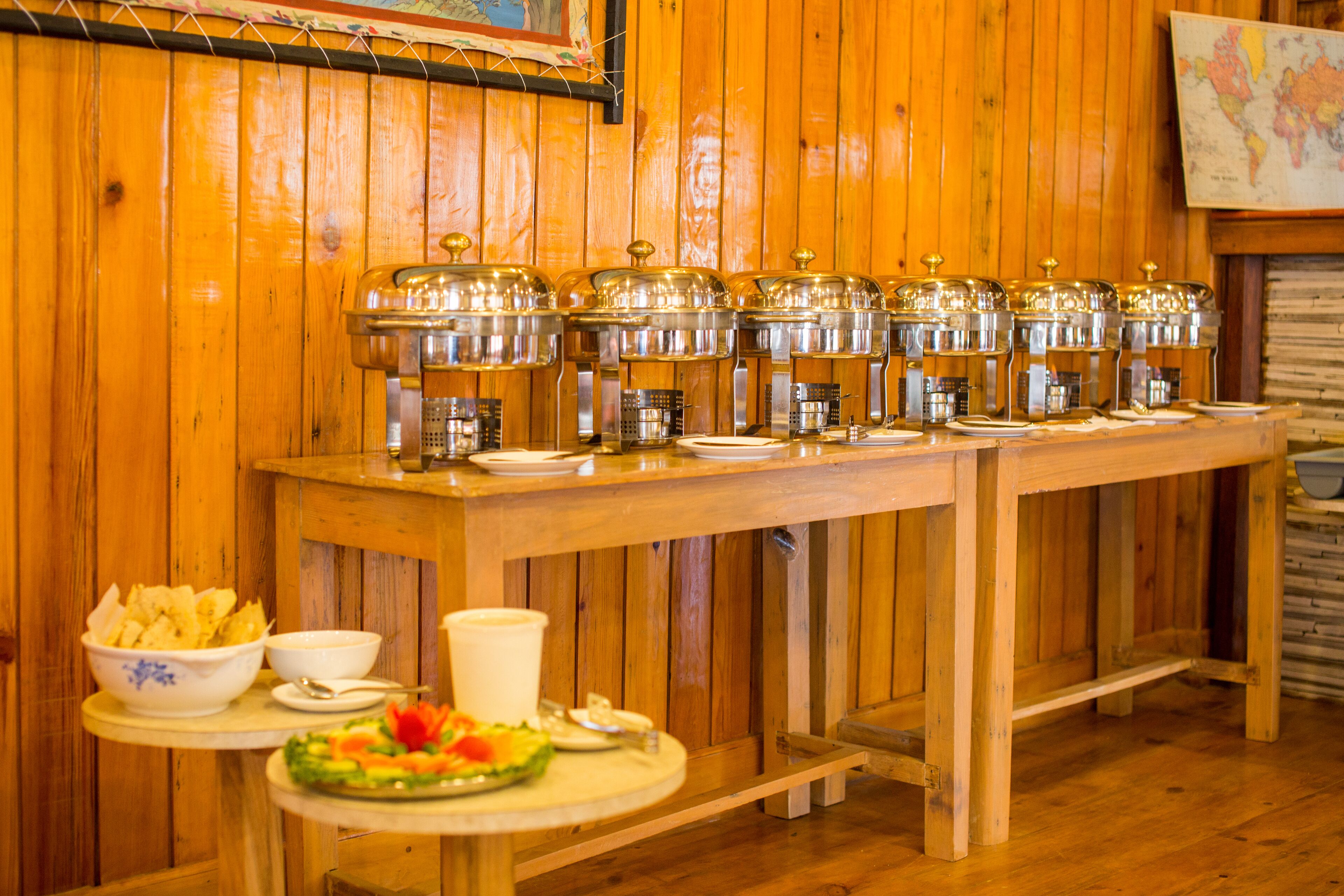 Disposição de buffet com diversas estações de serviço, uma pequena mesa com salada e um mapa na parede.