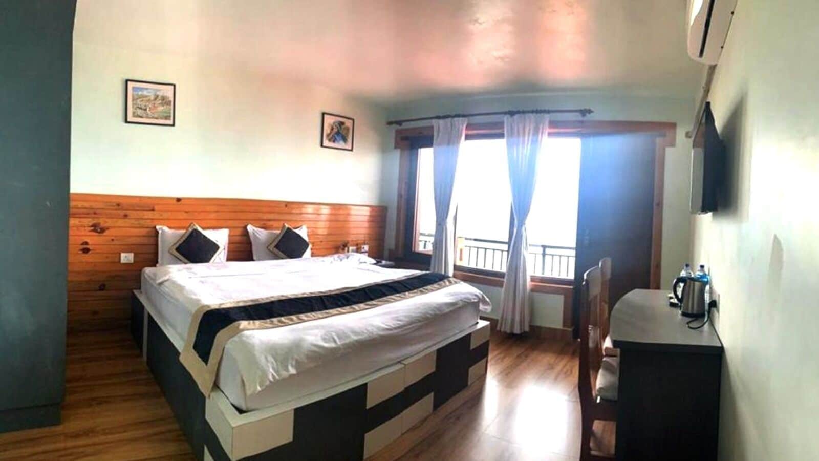 Quarto com cama, escrivaninha e cadeira. Possui duas janelas com cortinas.