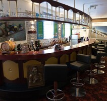 Uma área de bar com balcão curvo, vários bancos e uma variedade de garrafas e copos.