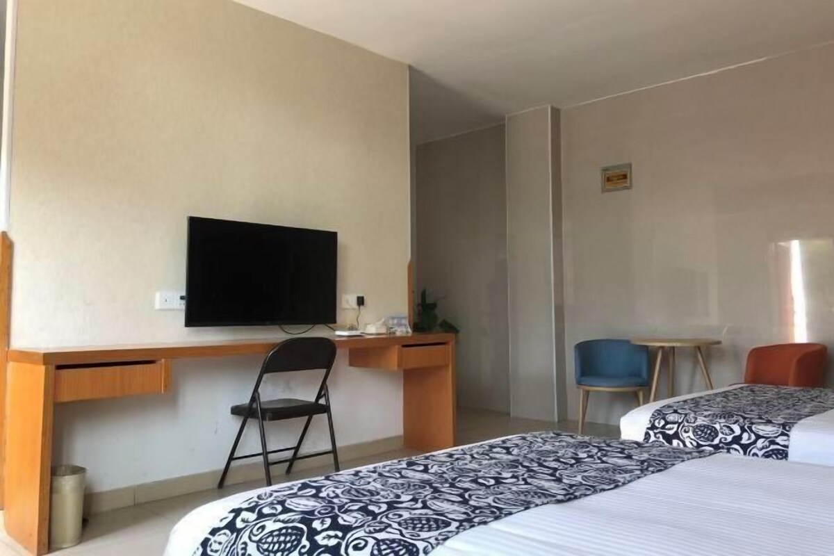 Quarto de hotel com uma cama, uma escrivaninha com cadeira, uma televisão e duas mesas de cabeceira.
