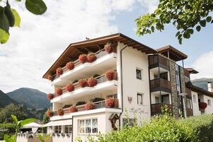 Hotel com vários andares e varandas decoradas com cestos de flores, com montanhas ao fundo.