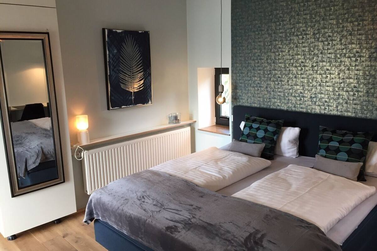 Quarto moderno com cama grande, espelho, radiador e parede texturizada.