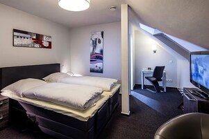 Quarto de hotel moderno com duas camas, uma escrivaninha, uma cadeira e uma televisão.