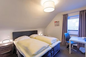 Quarto de hotel com cama, mesa de cabeceira, luminária, cadeira e janela com cortinas.