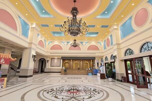 Um hall espaçoso com um lustre imponente, um balcão de recepção e um piso com padrão.