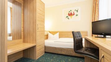 Quarto de hotel com uma cama, uma escrivaninha com televisão, uma cadeira e uma obra de arte na parede.