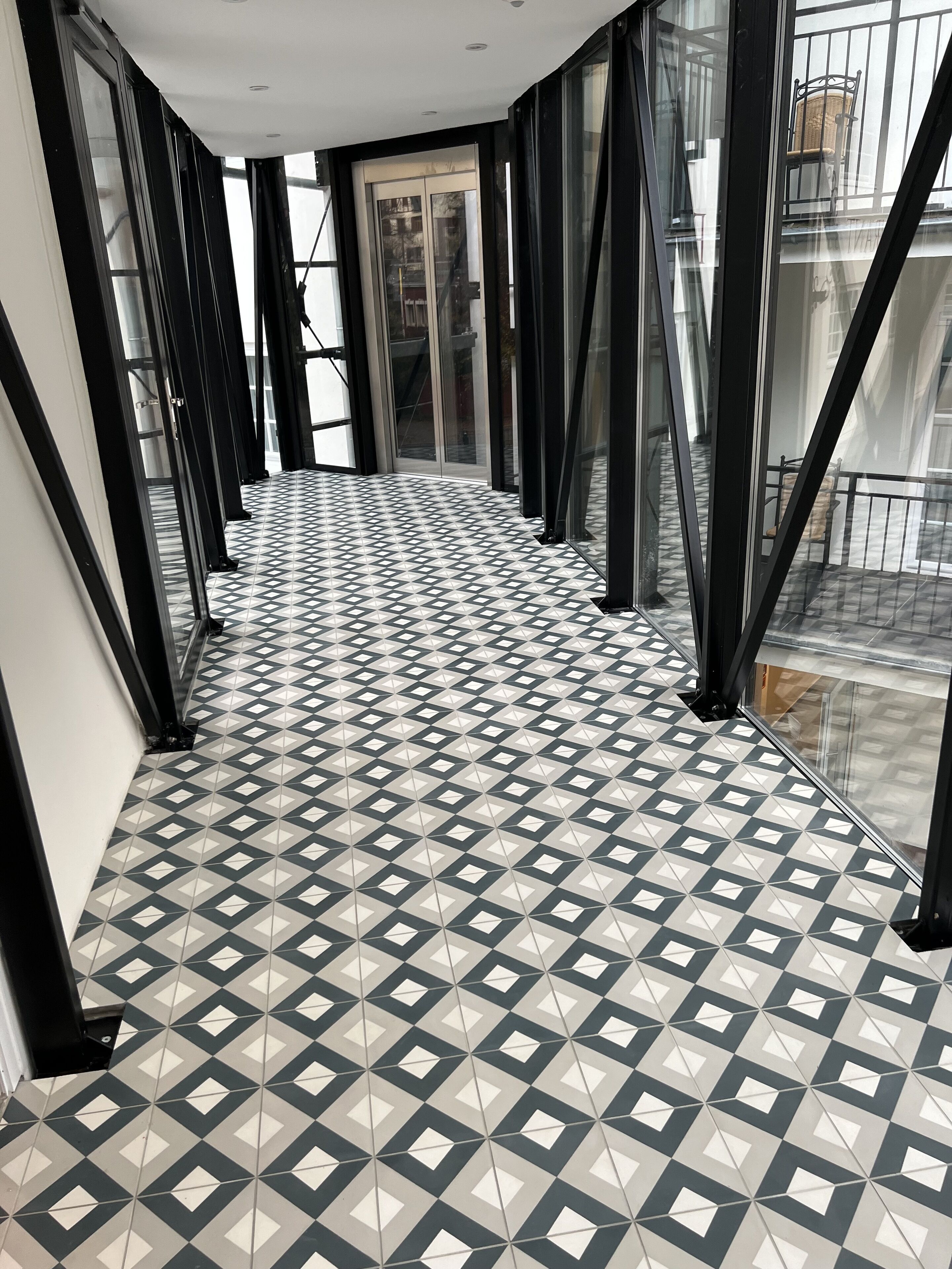 Um corredor com piso estampado e portas de vidro que dão para uma varanda.