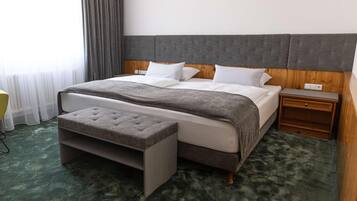 Quarto de hotel com uma cama grande, cabeceira de madeira, mesa de cabeceira e um banco.