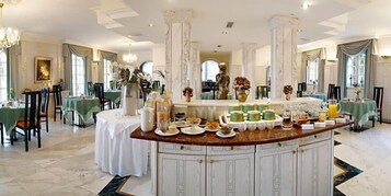 Uma área de refeições luxuosa com colunas de mármore, toalhas de mesa verdes e diversas opções de pequeno-almoço.