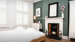Quarto com cama, penteadeira, lareira e janela com persianas.