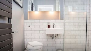 Uma casa de banho moderna com azulejos brancos tipo metrô, sanita branca, lavatório com espelho em cima e cabine de duche em vidro.