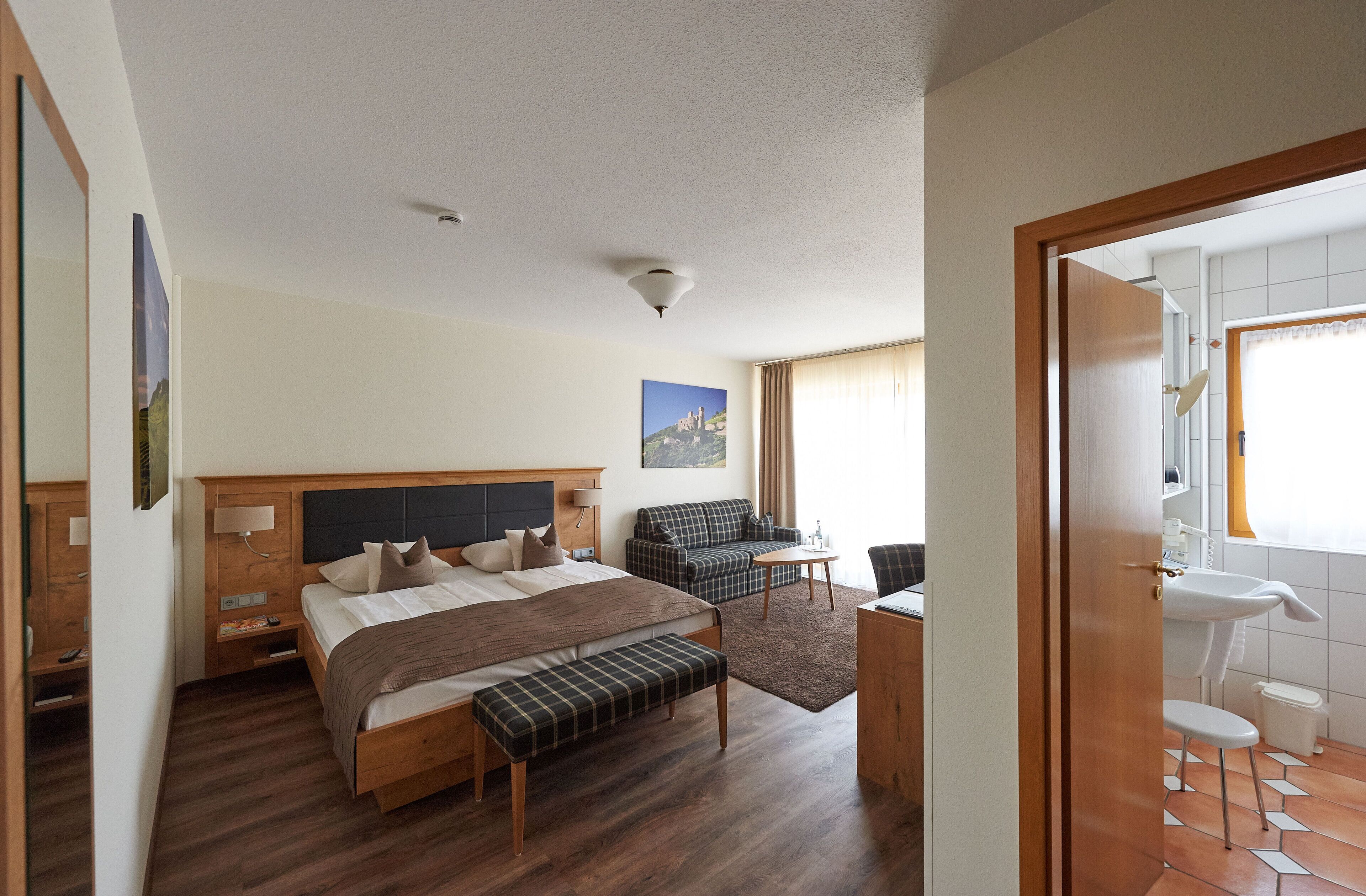 Quarto de hotel com cama, sofá, mesinha e banheiro visível através de uma porta aberta.